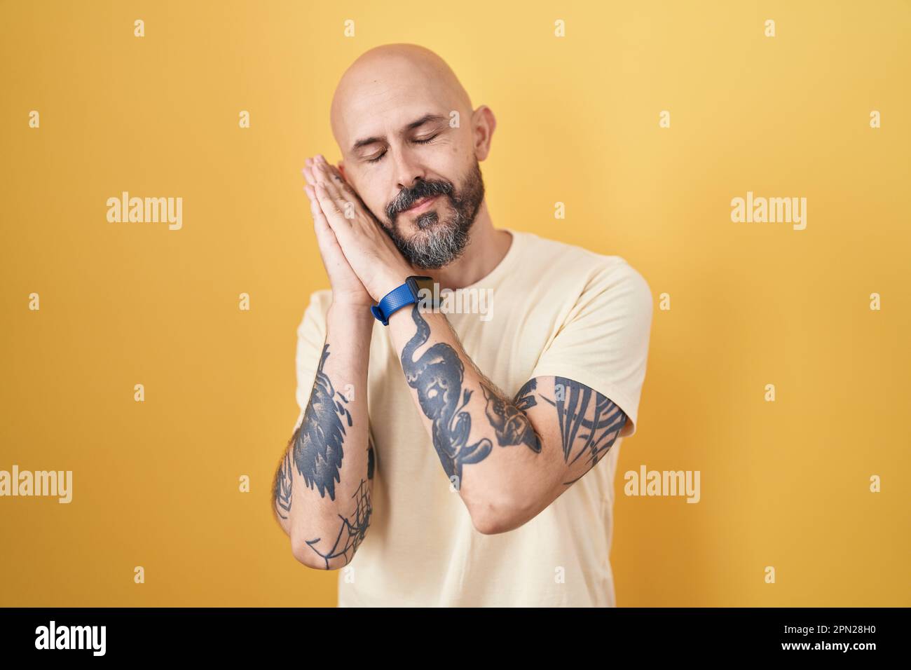 Hispanic man with tattoos standing over yellow background sleeping ...