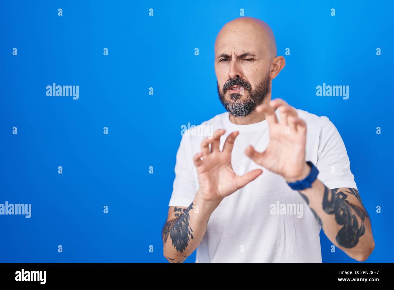 Hispanic man with tattoos standing over blue background disgusted ...