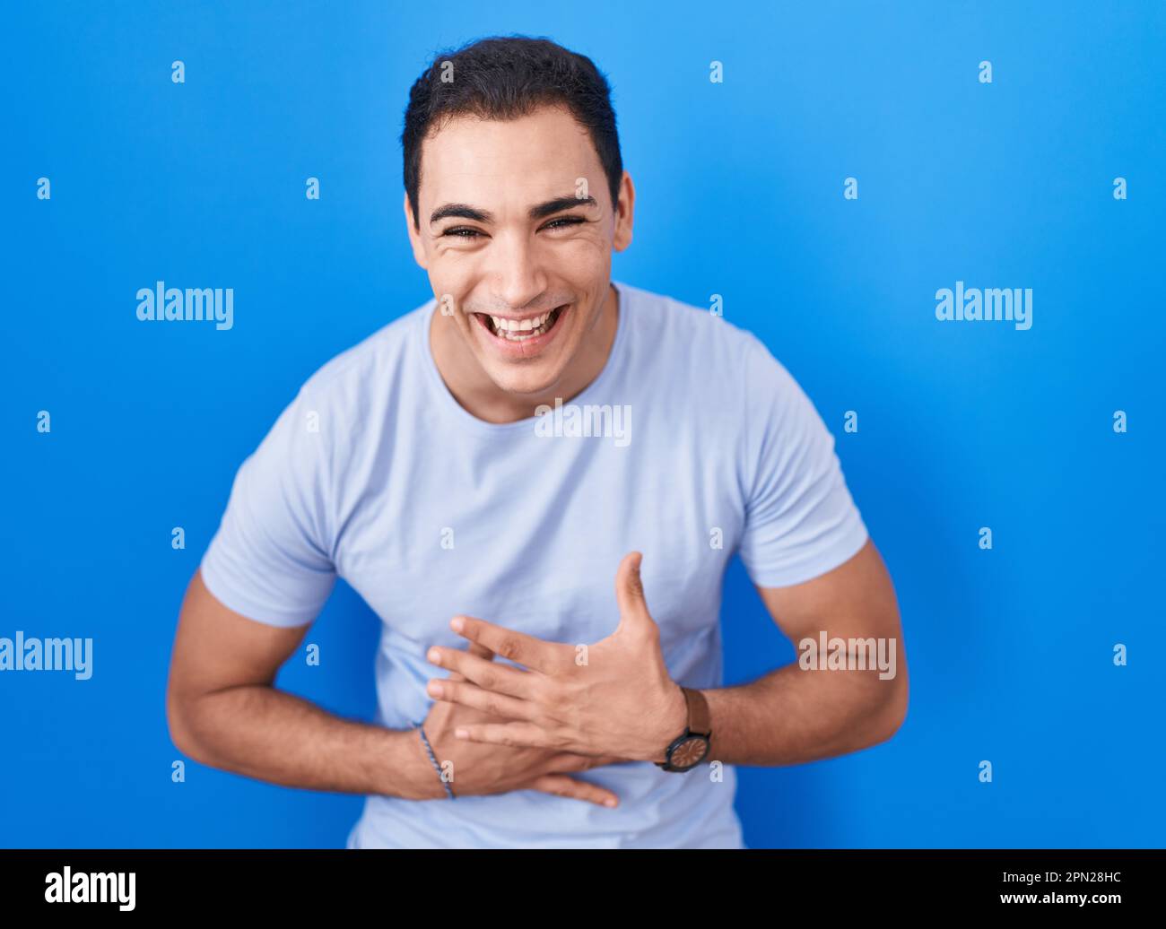 Young hispanic man standing over blue background smiling and laughing ...