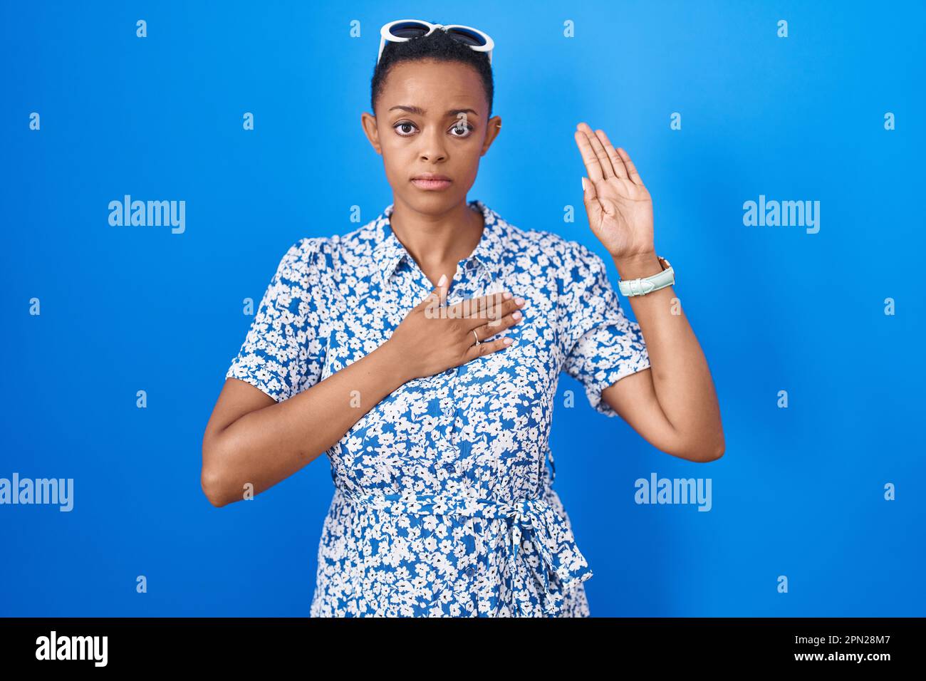 African american woman standing over blue background swearing with hand ...