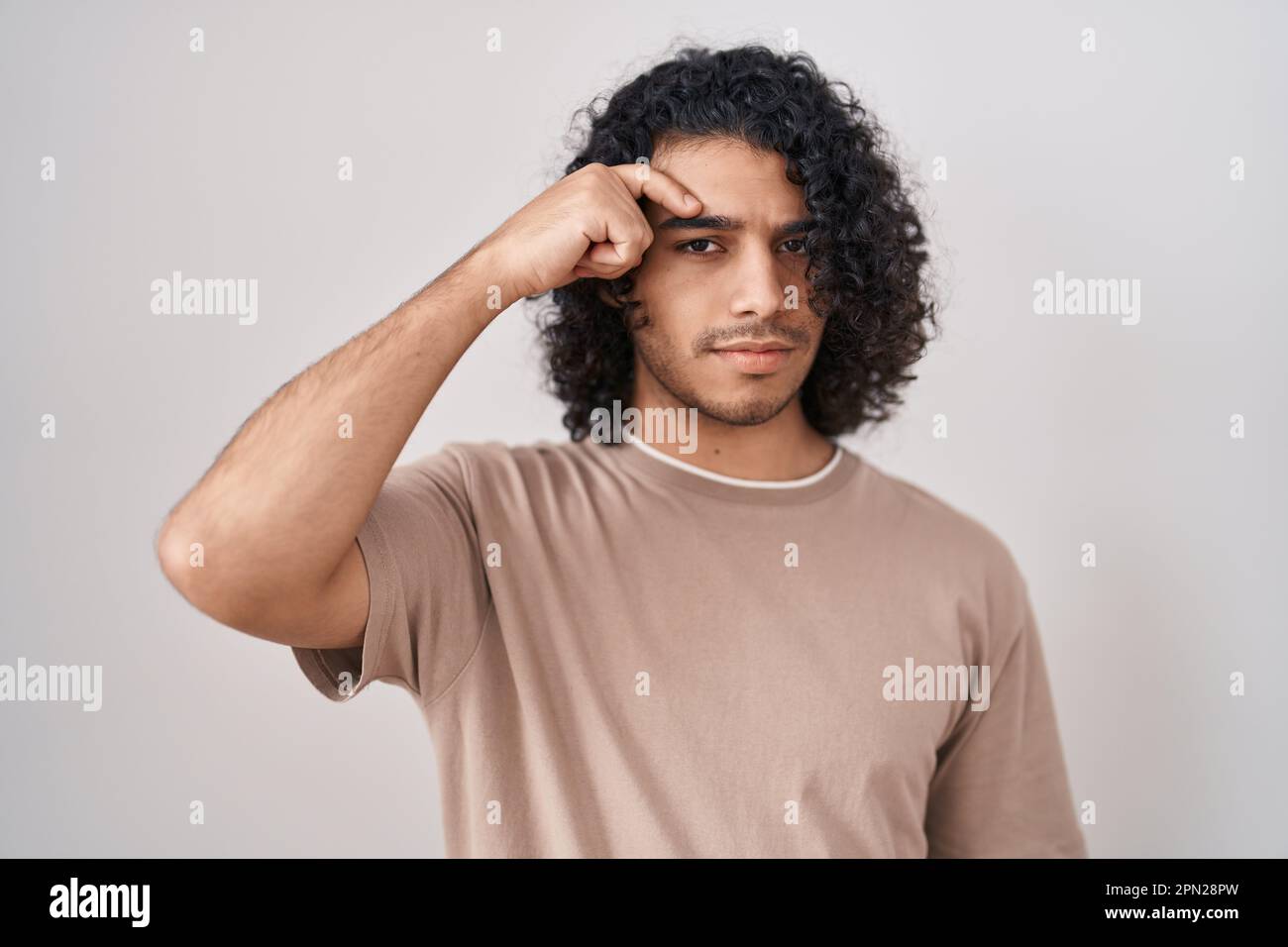 Hispanic man with curly hair standing over white background pointing ...