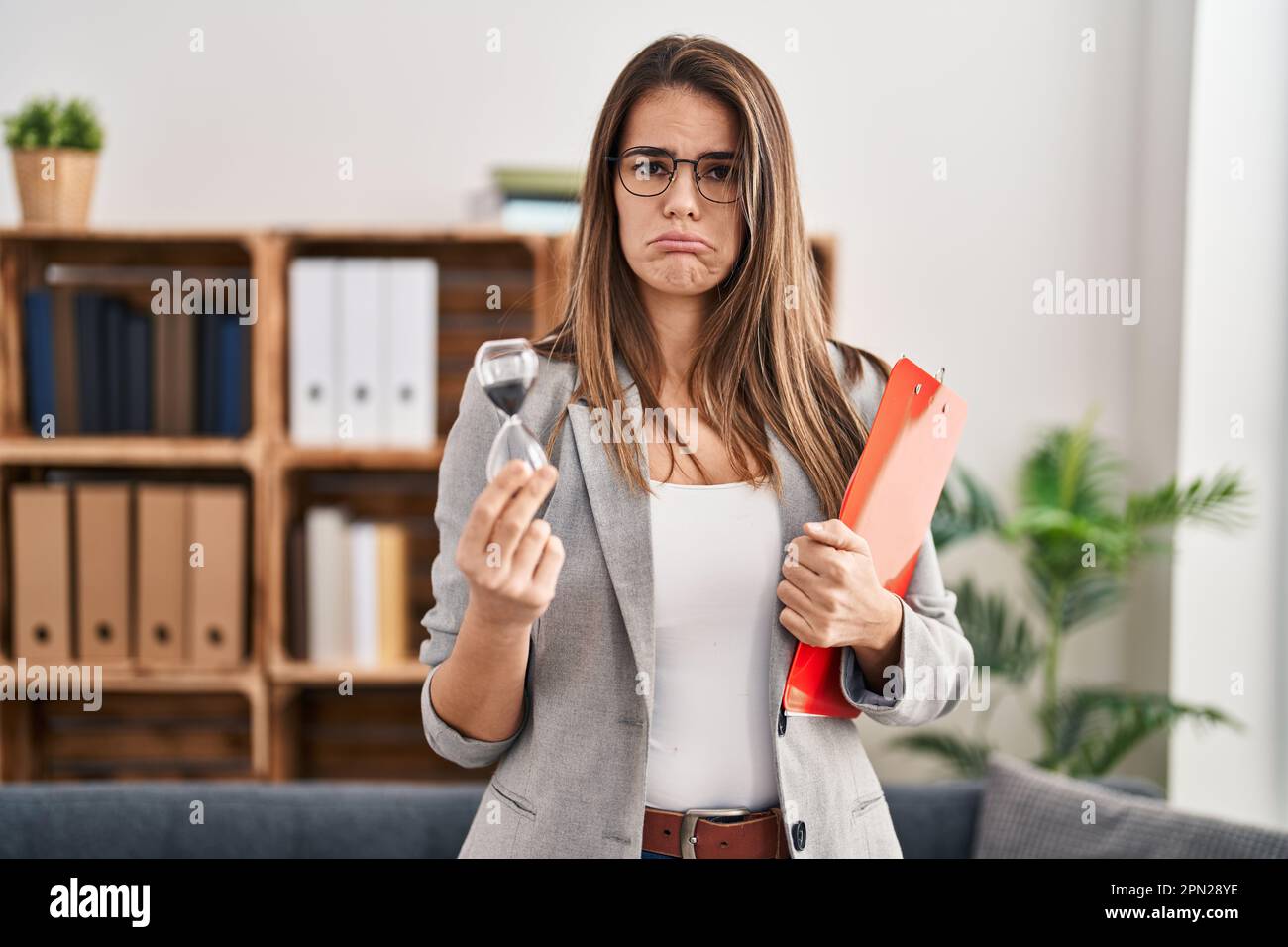 Beautiful woman working at therapy office holding sand clock depressed ...