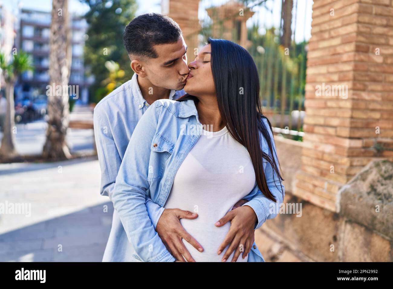 Young latin couple expecting baby hugging each other and kissing at street Stock Photo - Alamy