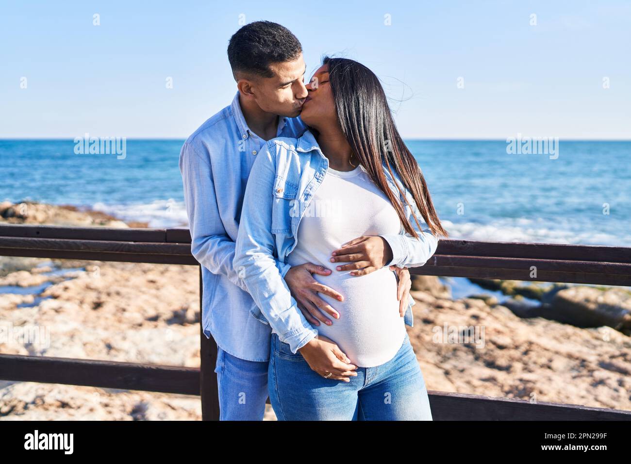 Young latin couple expecting baby hugging each other and kissing at ...