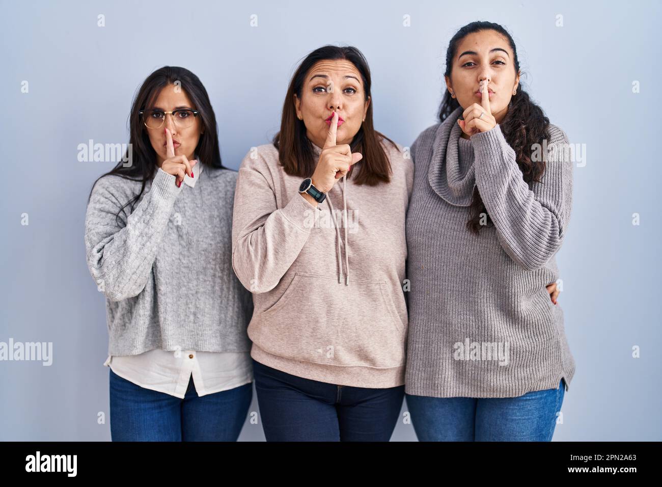 Mother and two daughters standing over blue background asking to be ...