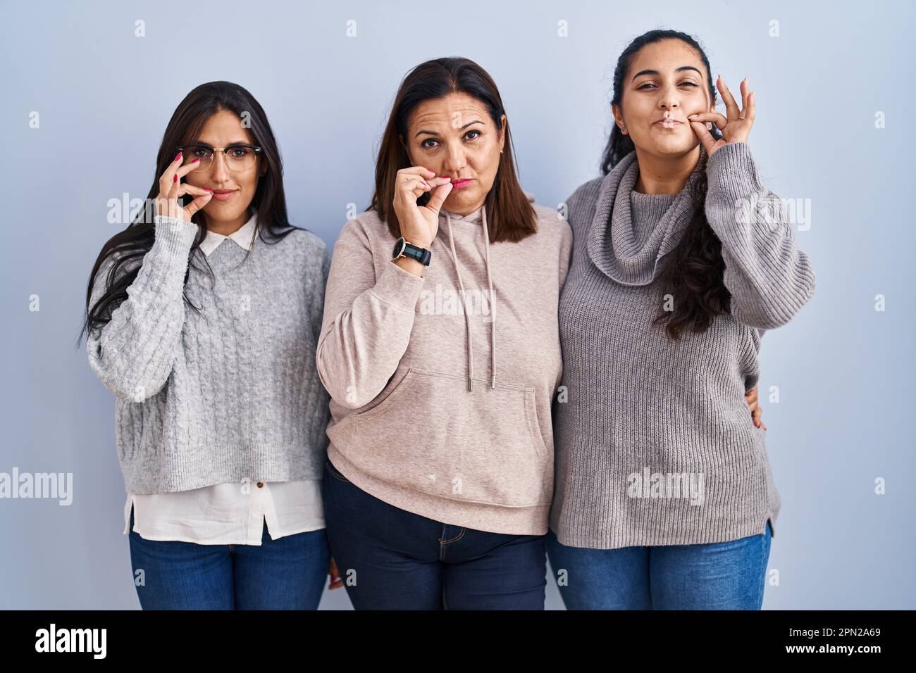Mother and two daughters standing over blue background mouth and lips ...