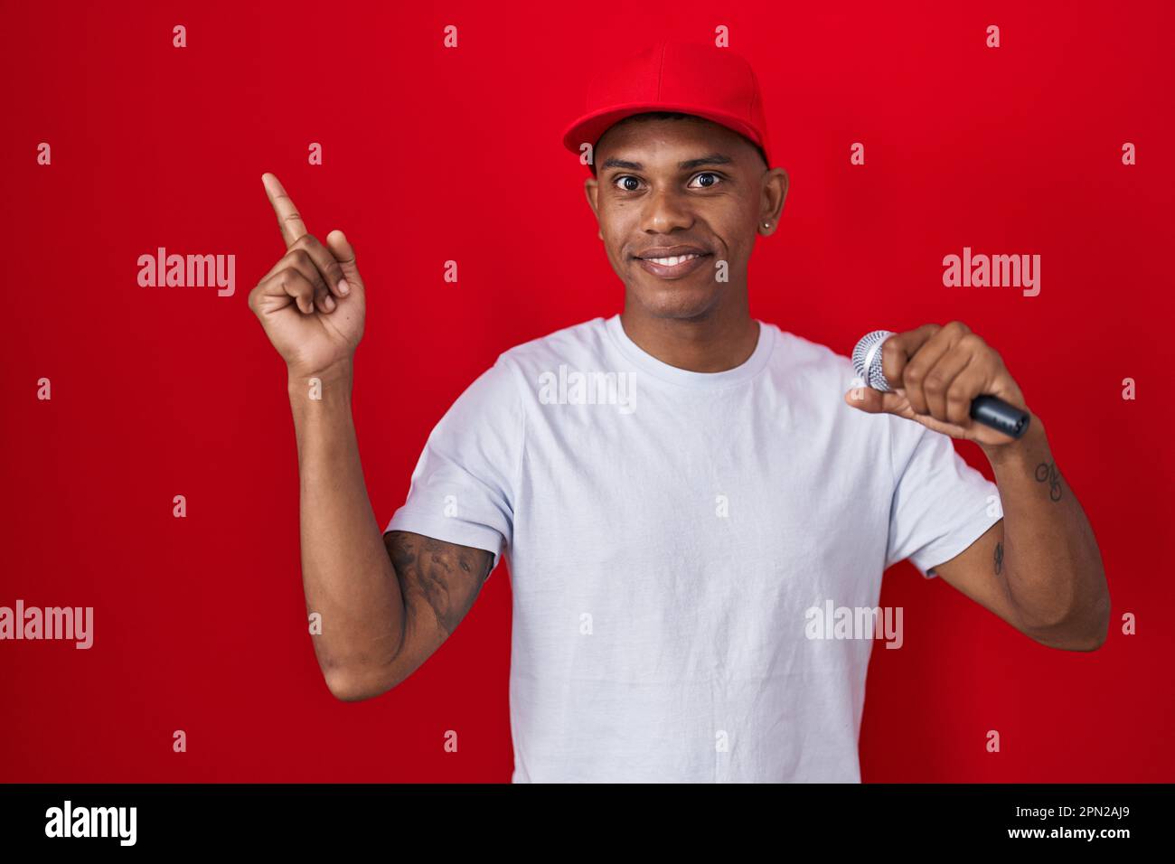 Young hispanic man singing song using microphone smiling happy pointing ...