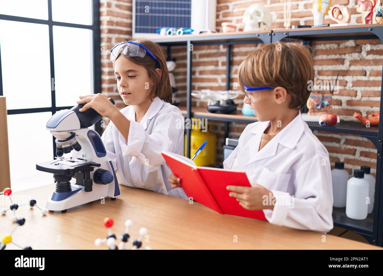 Adorable boys students using microscope writing notes at laboratory ...
