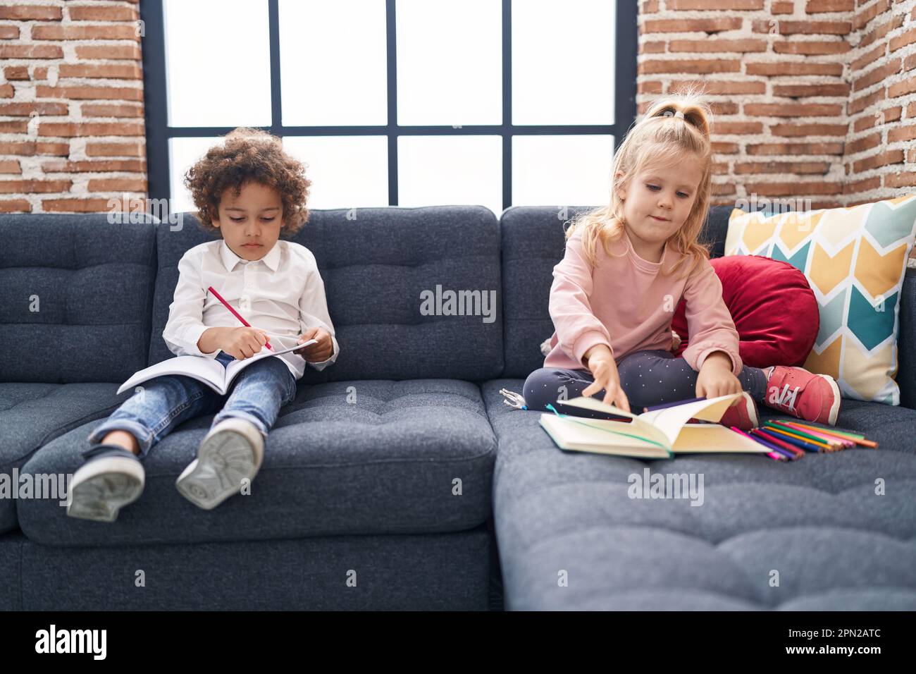 Adorable boy and girl students sitting on sofa drawing on notebook at ...