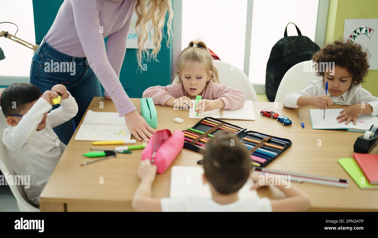 Woman and group of kids having lesson sitting on table at classroom ...