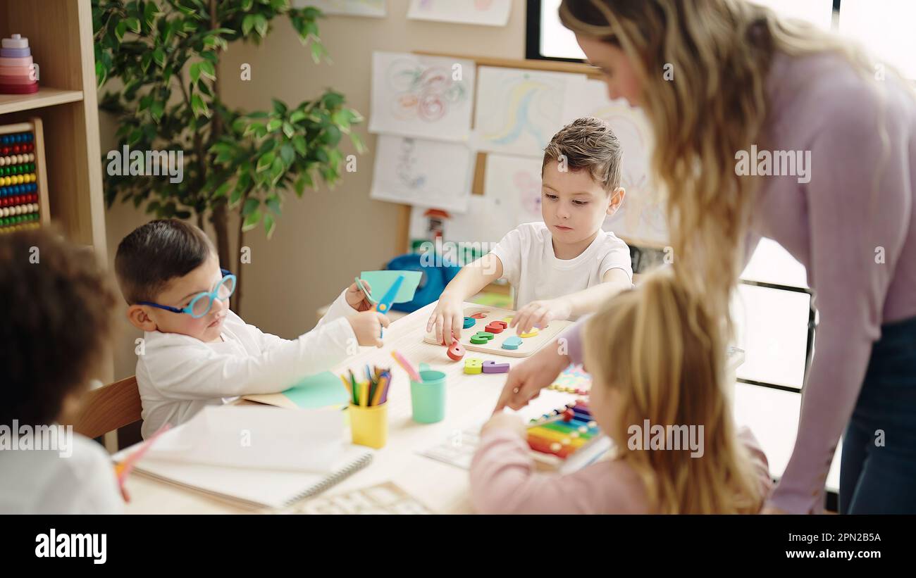 Woman and group of kids having lesson sitting on table at kindergarten ...