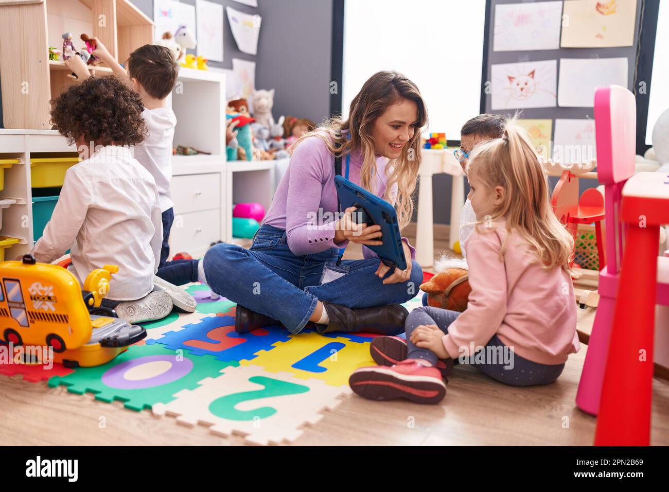Woman and group of kids having lesson using touchpad at kindergarten ...