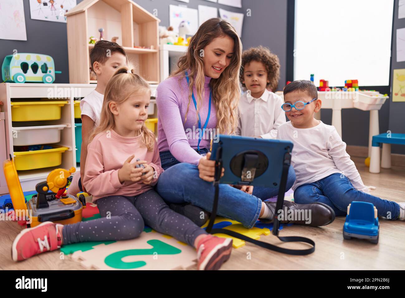 Woman and group of kids having lesson using touchpad at kindergarten ...