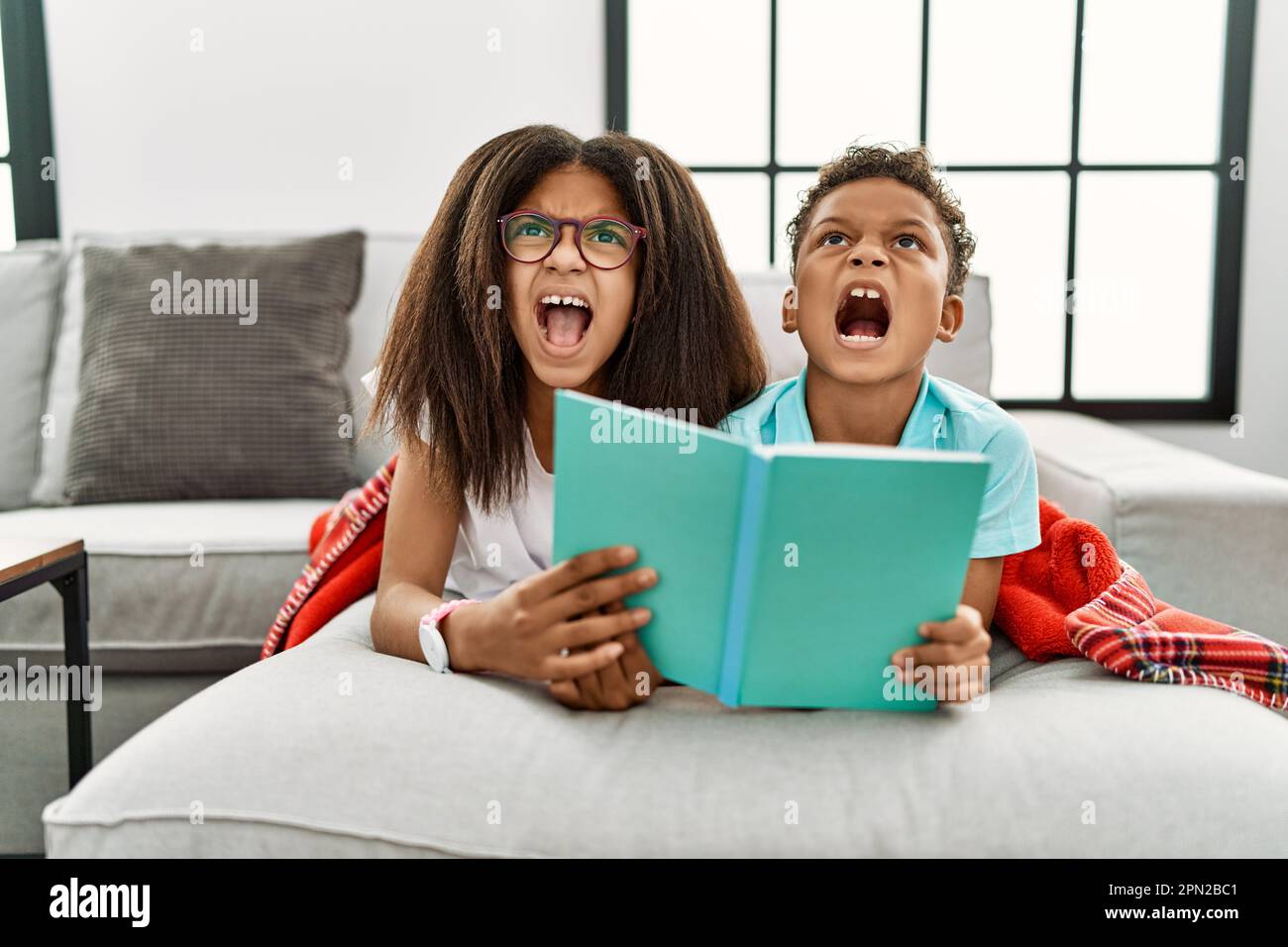 Two siblings lying on the sofa reading a book angry and mad screaming ...