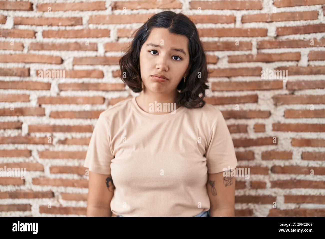 Young hispanic woman standing over bricks wall depressed and worry for ...