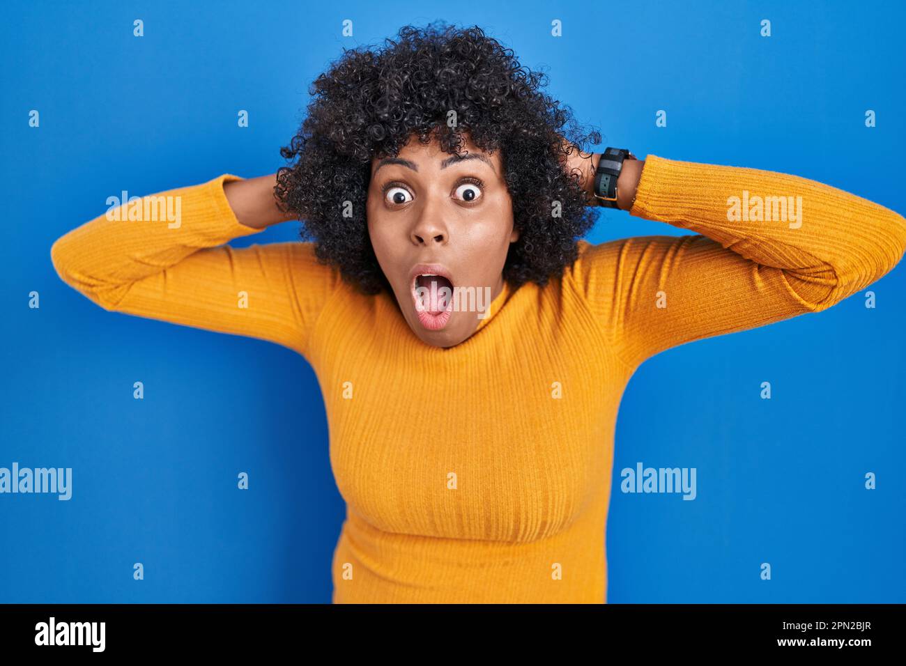Black woman with curly hair standing over blue background crazy and ...
