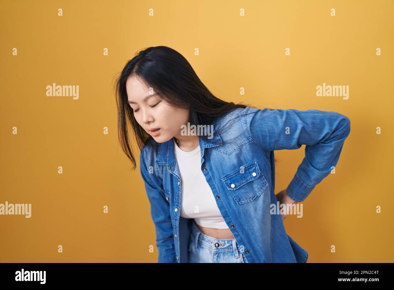 Young asian woman standing over yellow background suffering of backache ...