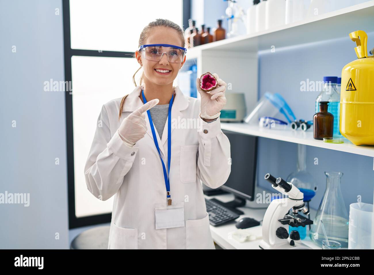 Young woman working at scientist laboratory holding geode smiling happy ...