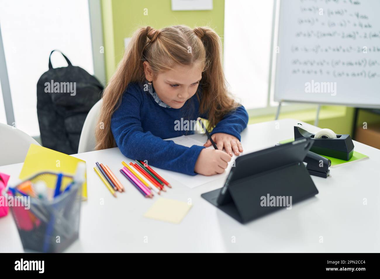 Adorable blonde girl student using touchpad writing notes at classroom ...