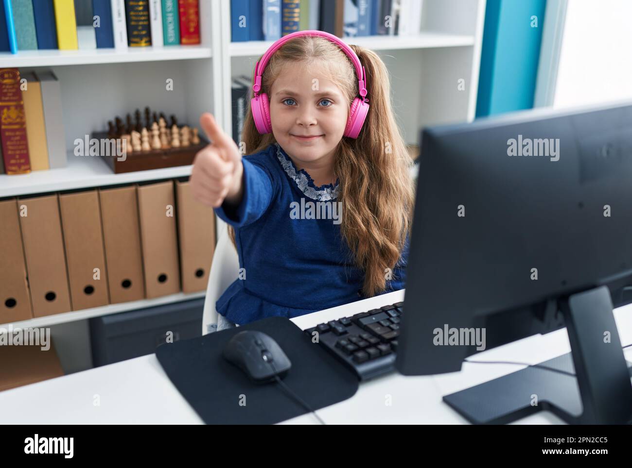 Adorable blonde girl student using computer and headphones doing thumb ...