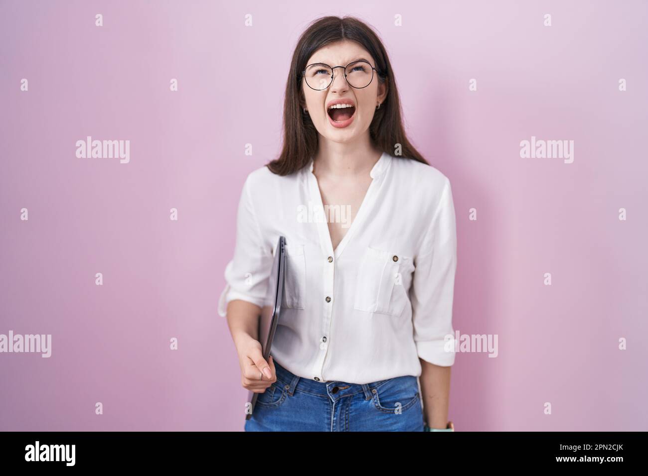 Young caucasian woman holding laptop angry and mad screaming frustrated ...