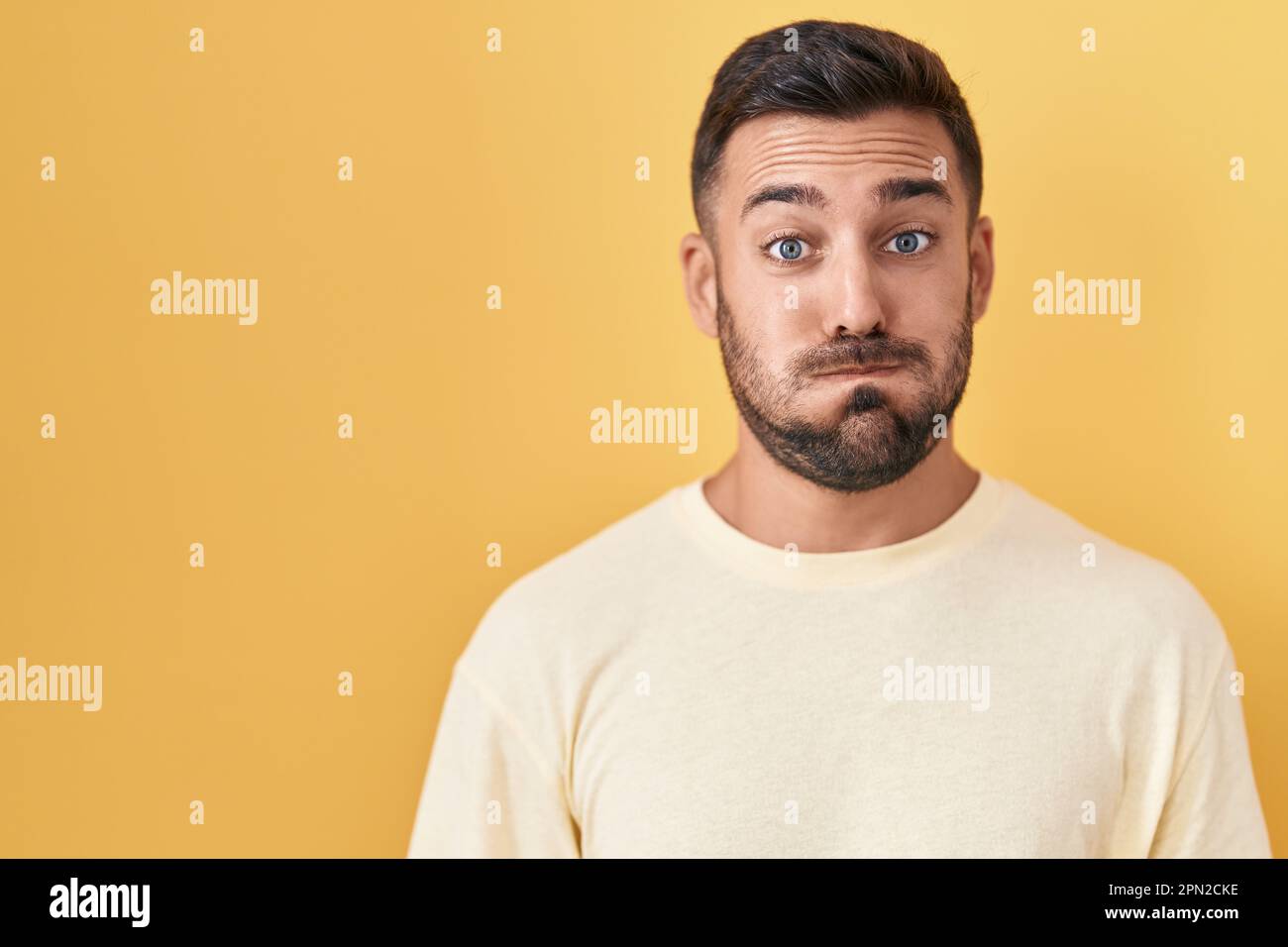 Handsome hispanic man standing over yellow background puffing cheeks ...