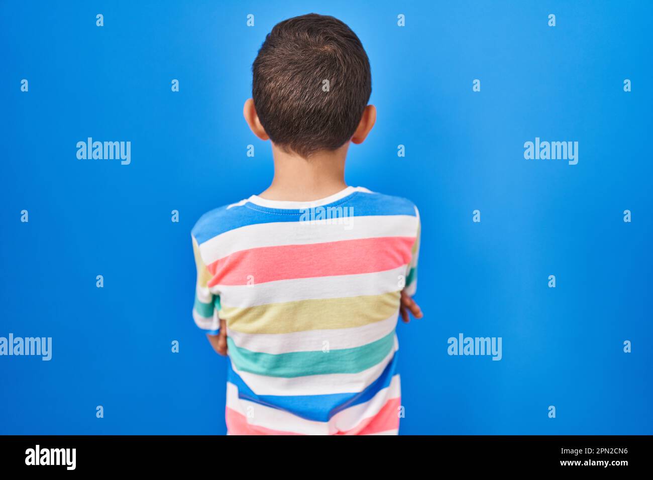 Young caucasian kid standing over blue background standing backwards ...