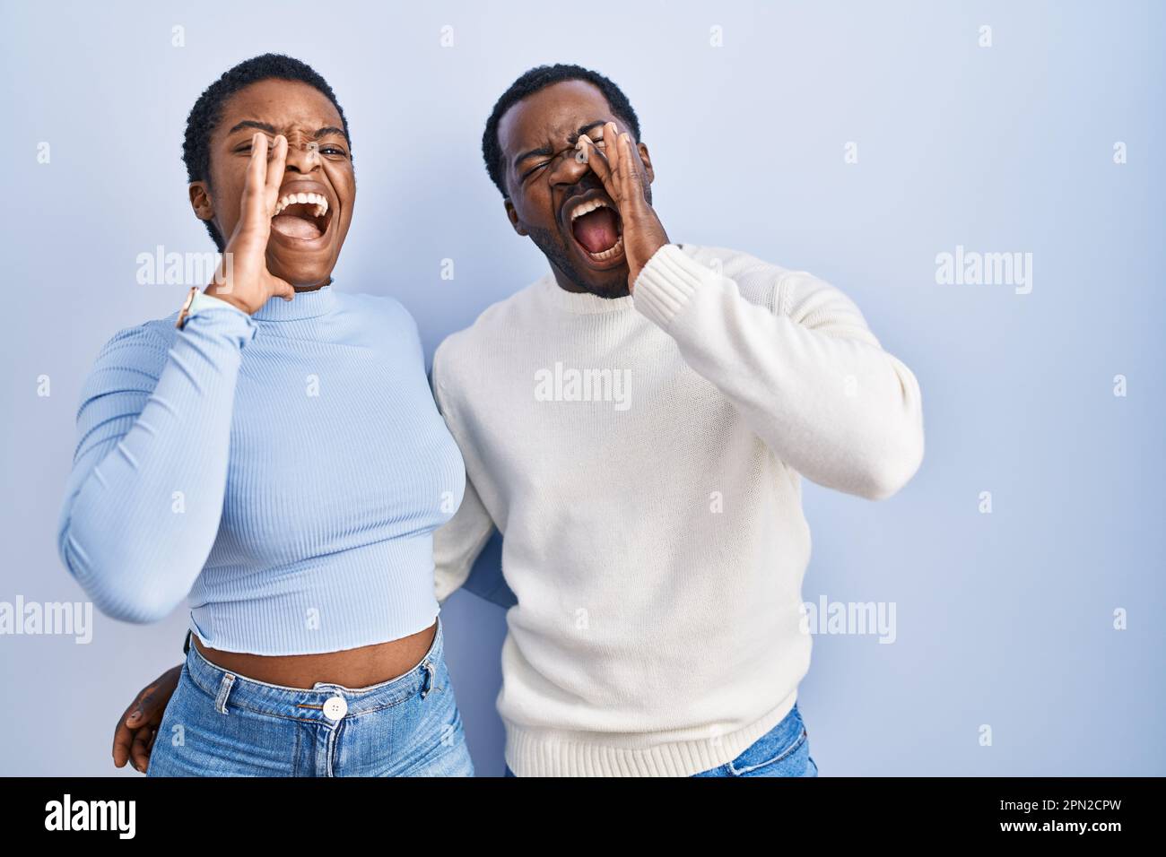 Young african american couple standing over blue background shouting ...