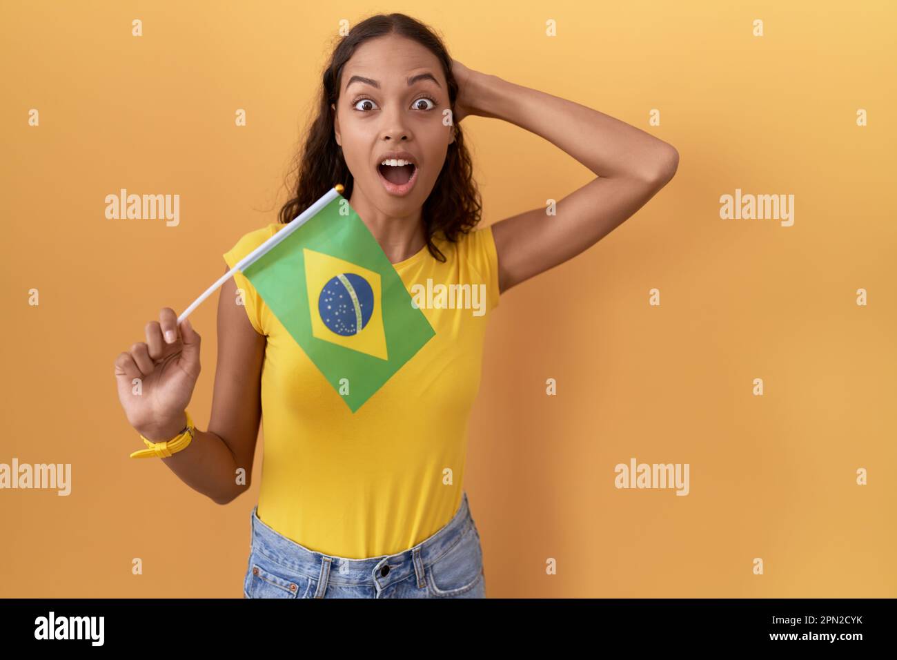 Young hispanic woman holding brazil flag crazy and scared with hands on ...