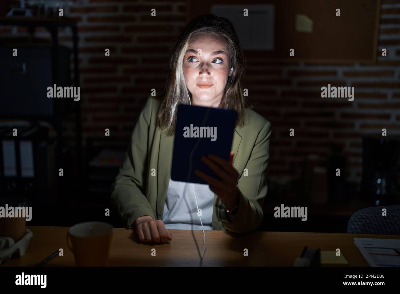Blonde caucasian woman working at the office at night smiling looking ...