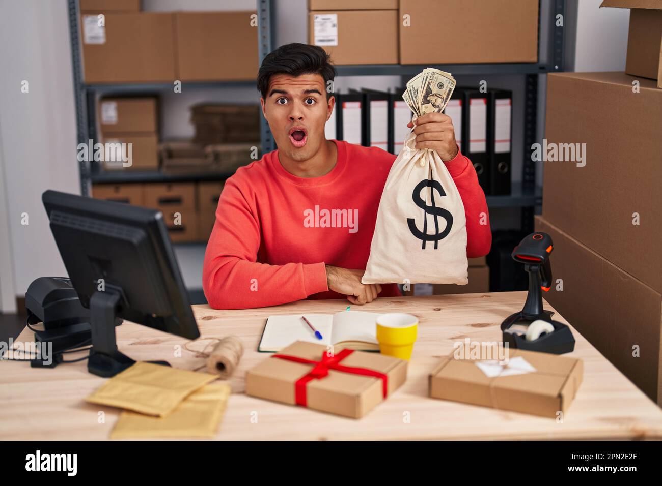 Hispanic man working at small business ecommerce holding money bag ...