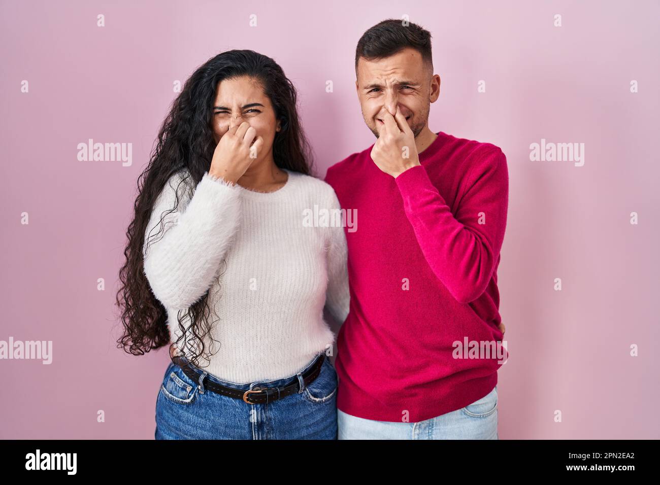 Young hispanic couple standing over pink background smelling something ...