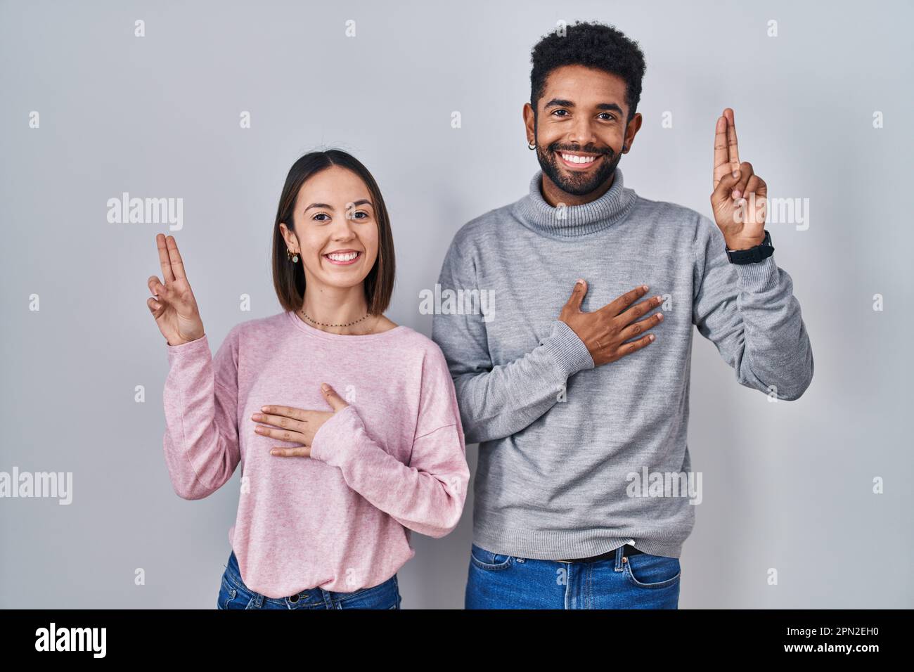 Young hispanic couple standing together smiling swearing with hand on ...
