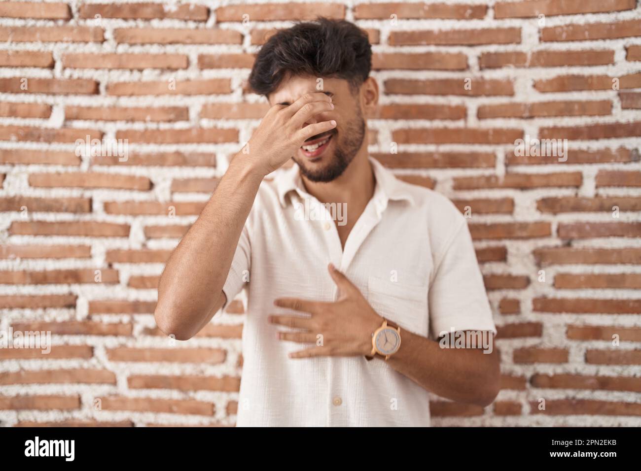 Arab man with beard standing over bricks wall background smelling ...