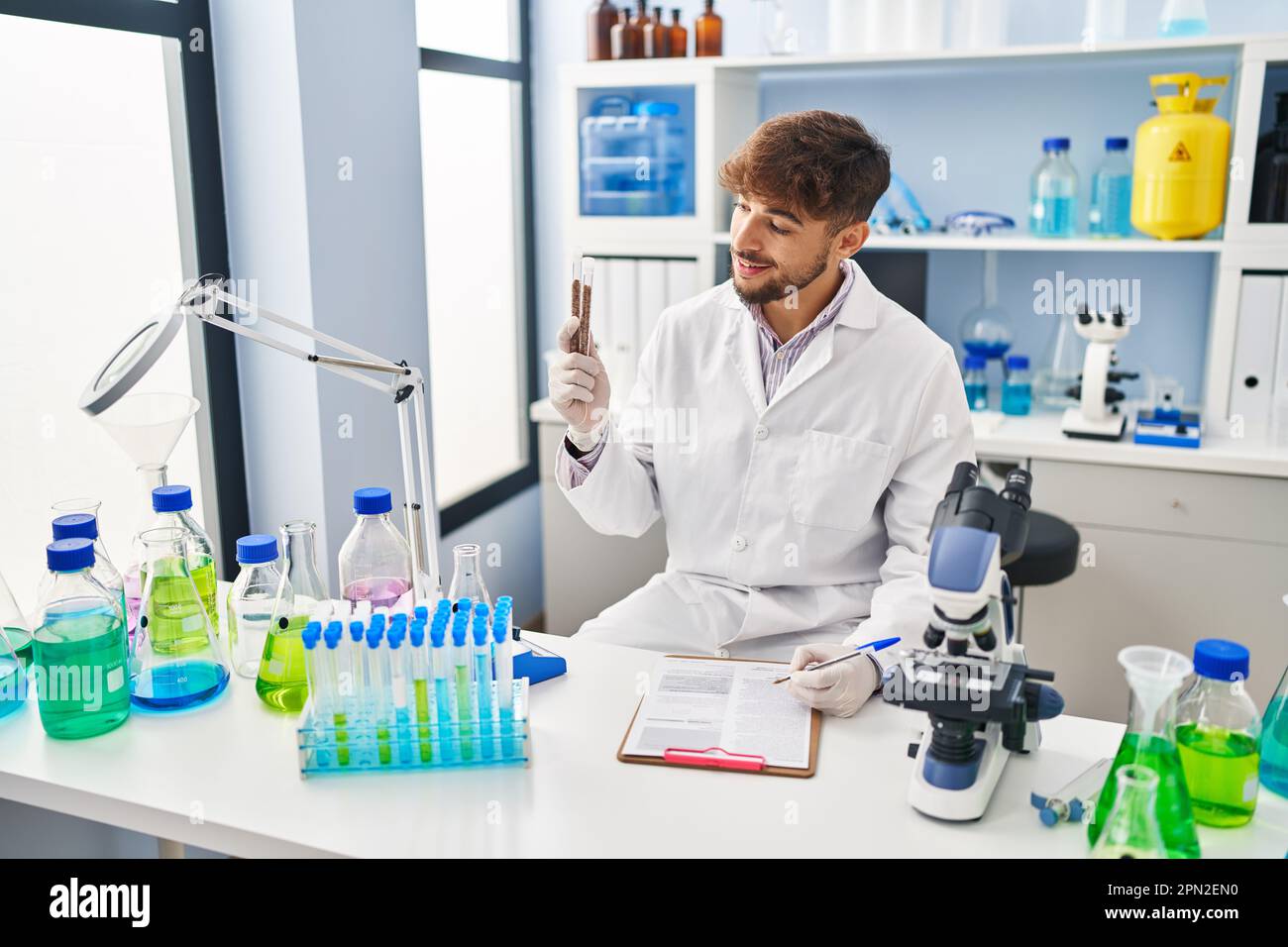 Young arab man scientist write on document analysing lentils test tube ...