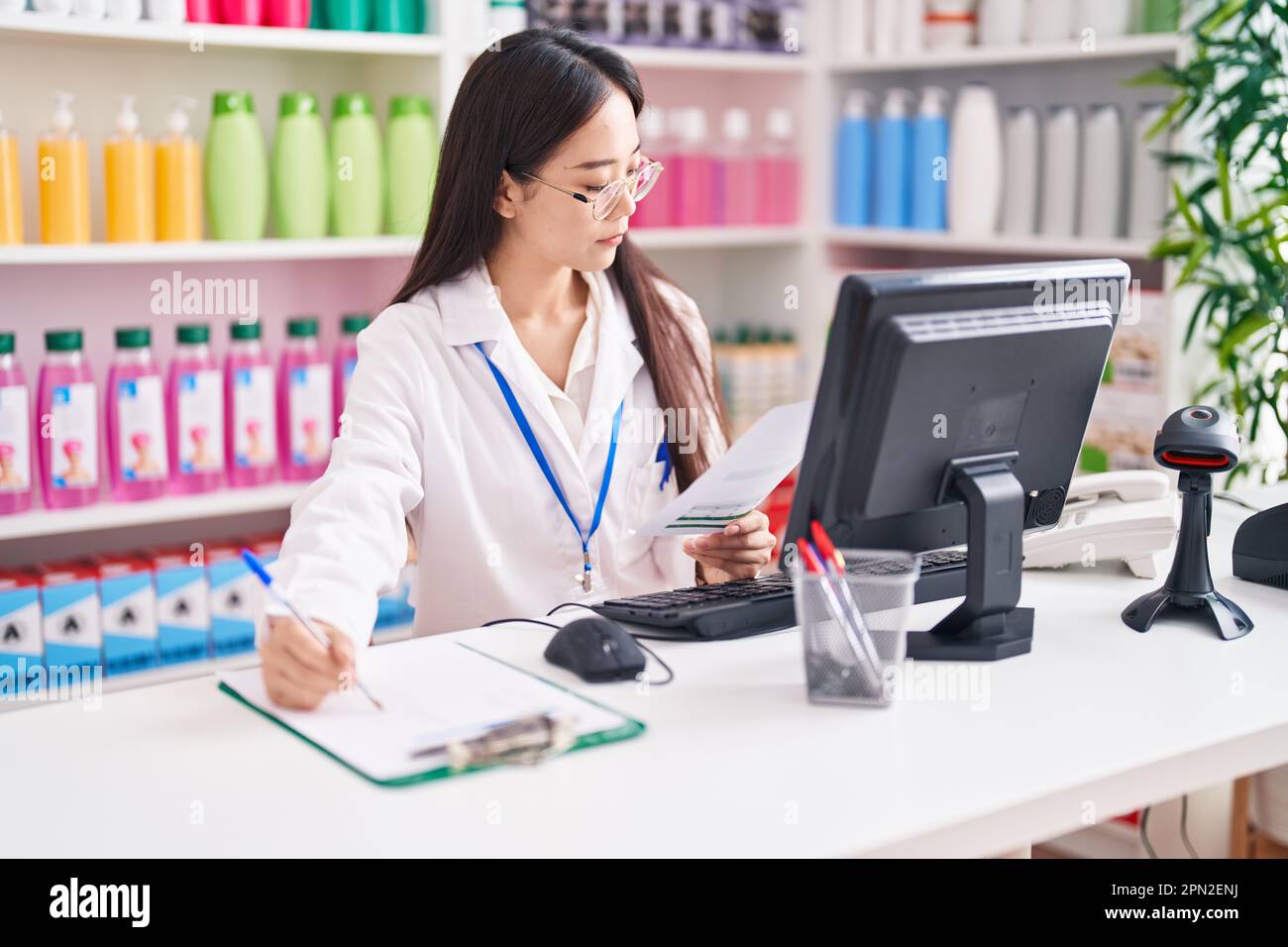 Young chinese woman pharmacist writing on document reading medical ...