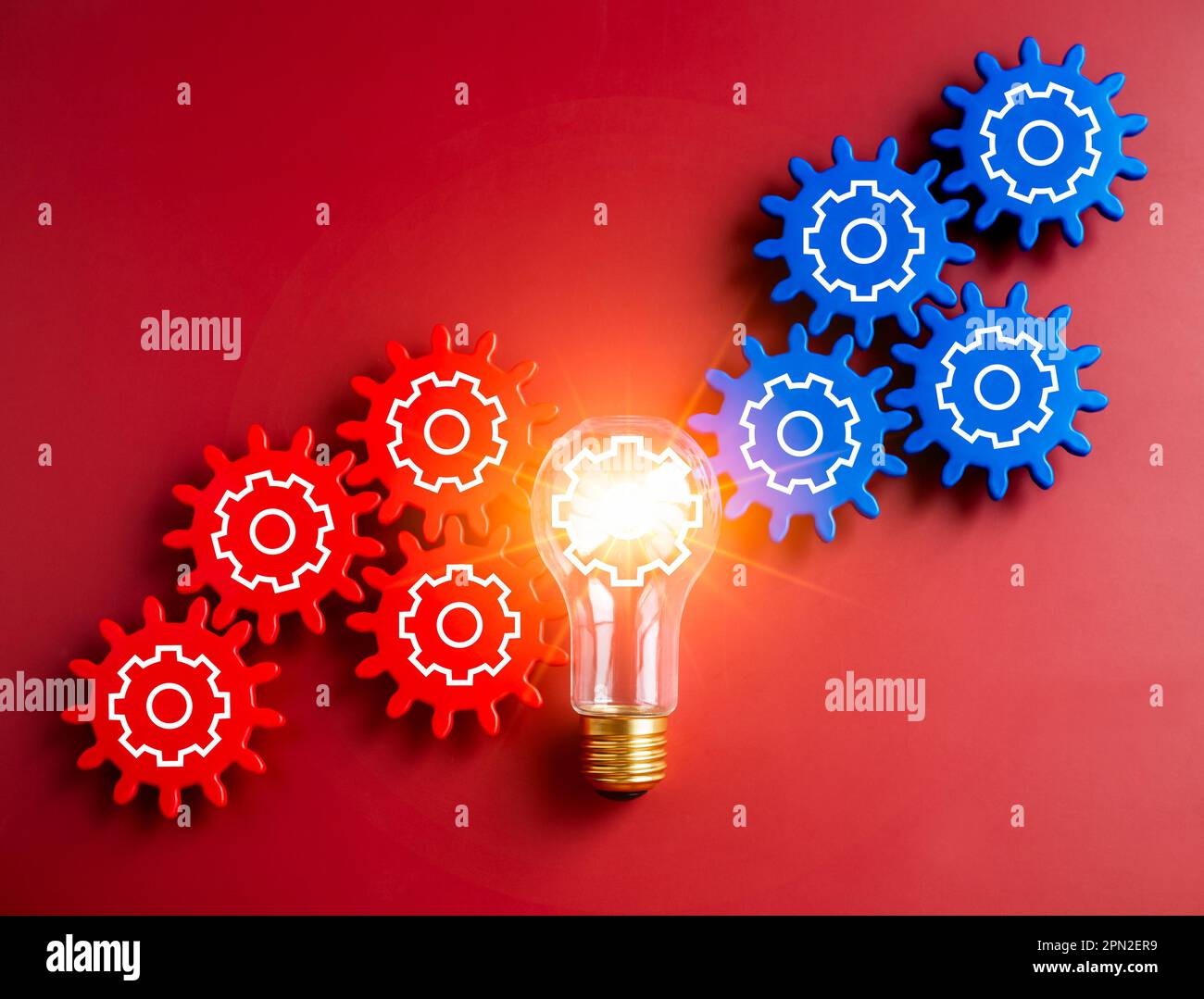Glowing light bulb connected between blue and red gear wheels on red ...