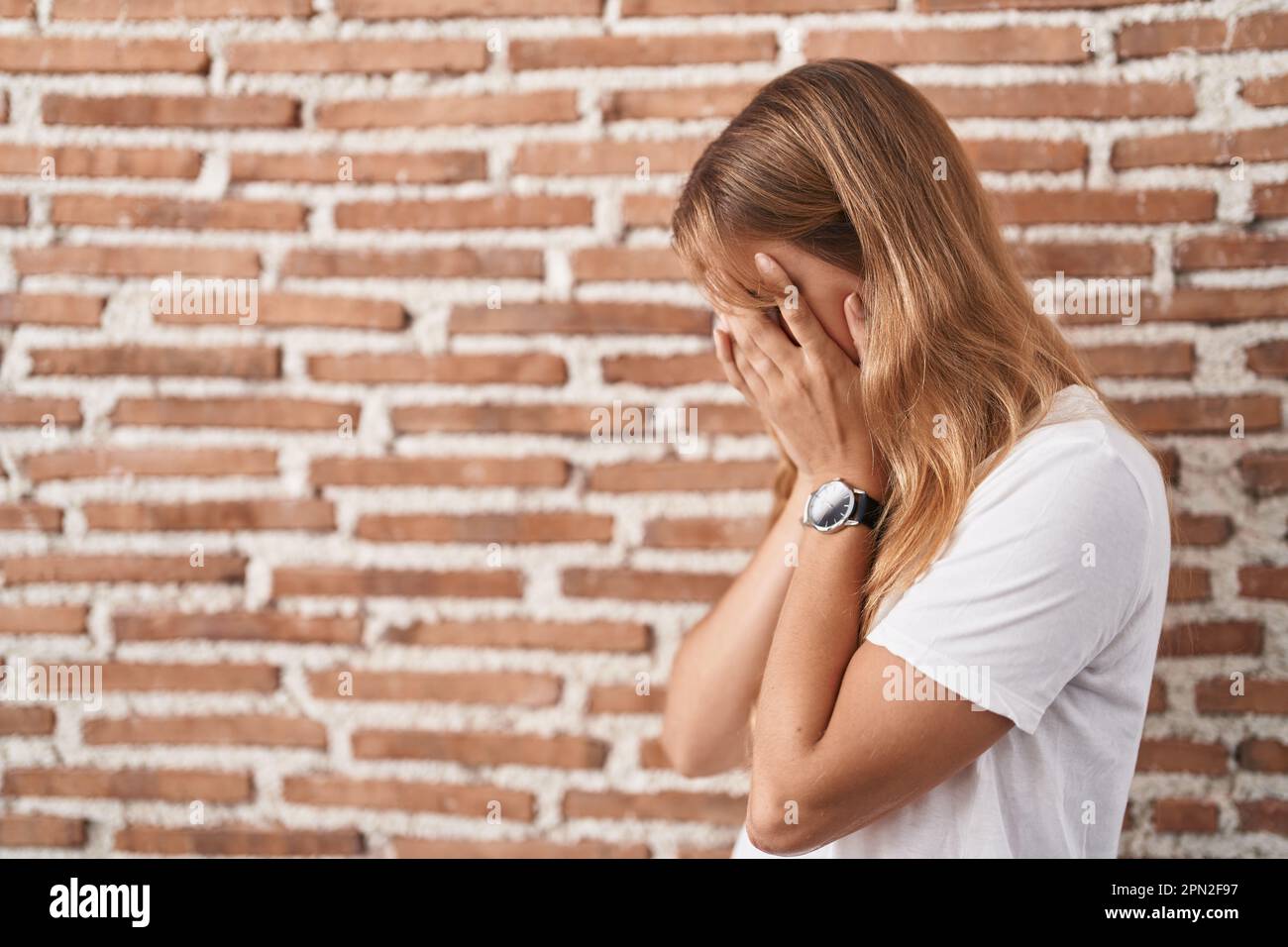 Young caucasian woman standing over bricks wall with sad expression ...