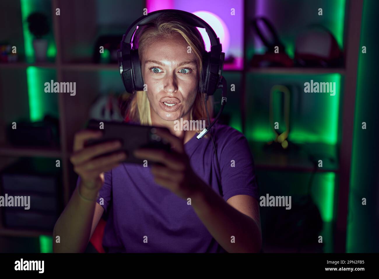 Young gamer woman playing video games with smartphone scared and amazed ...