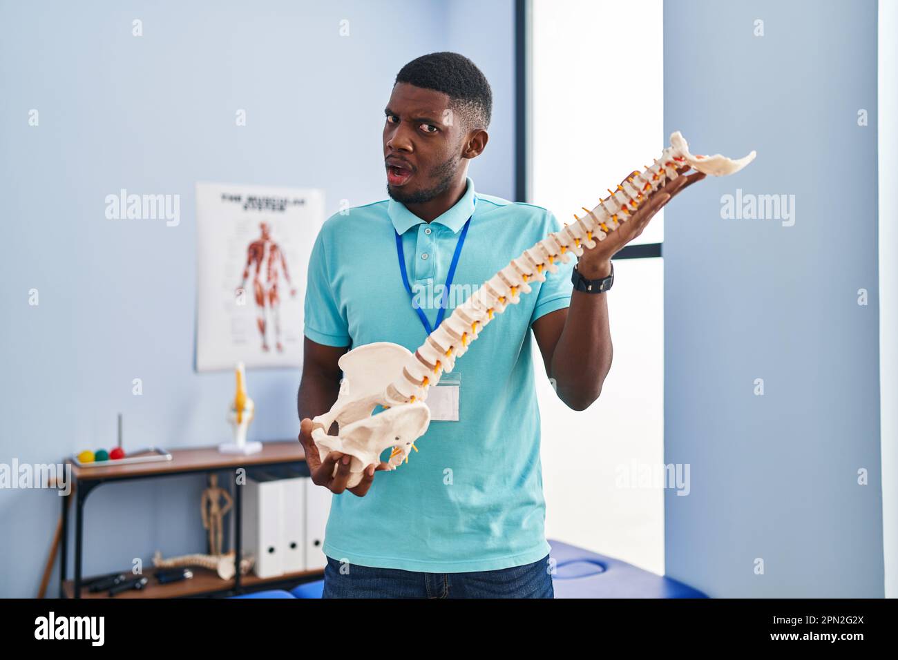 African american man holding anatomical model of spinal column in shock ...