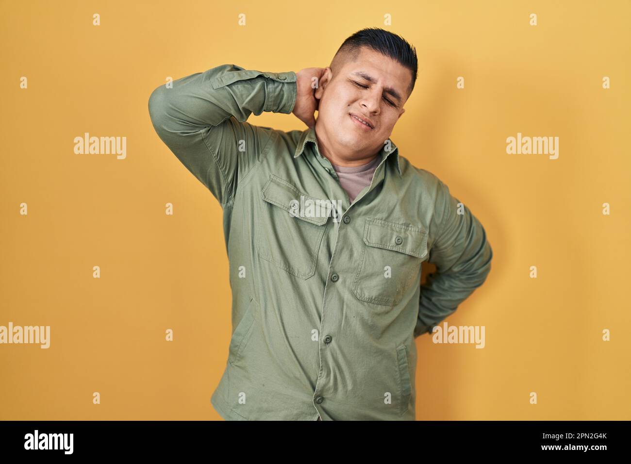 Hispanic young man standing over yellow background suffering of neck ...