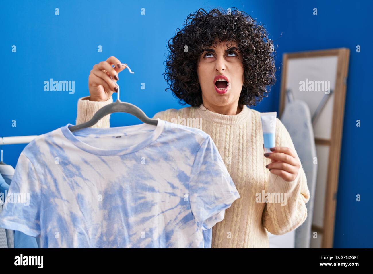 Young brunette woman with curly hair dyeing tye die t shirt angry and ...