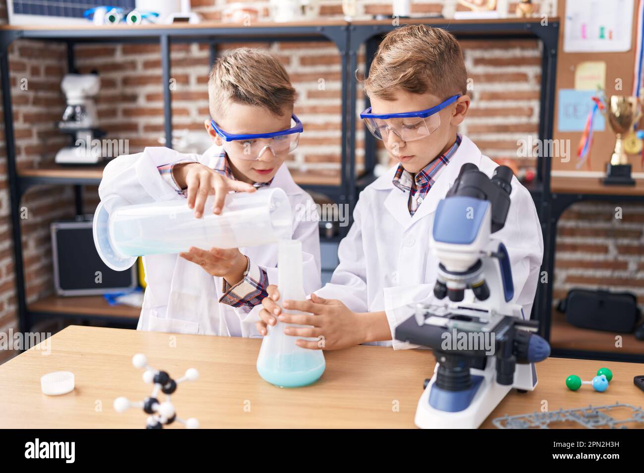 Adorable boys student pouring liquid on test tube at laboratory ...