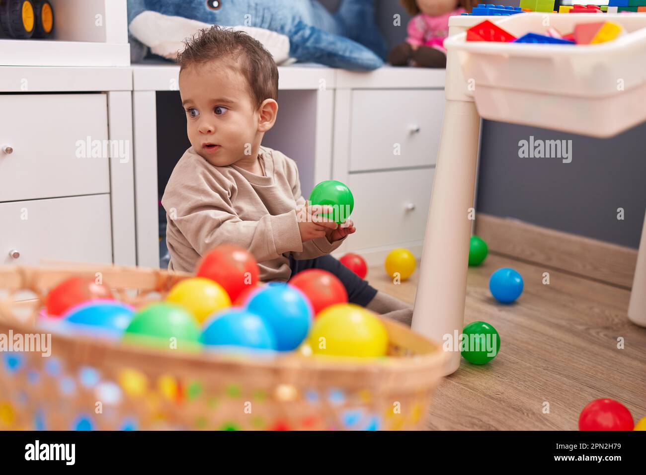 Adorable hispanic boy playing with balls sitting on floor at ...