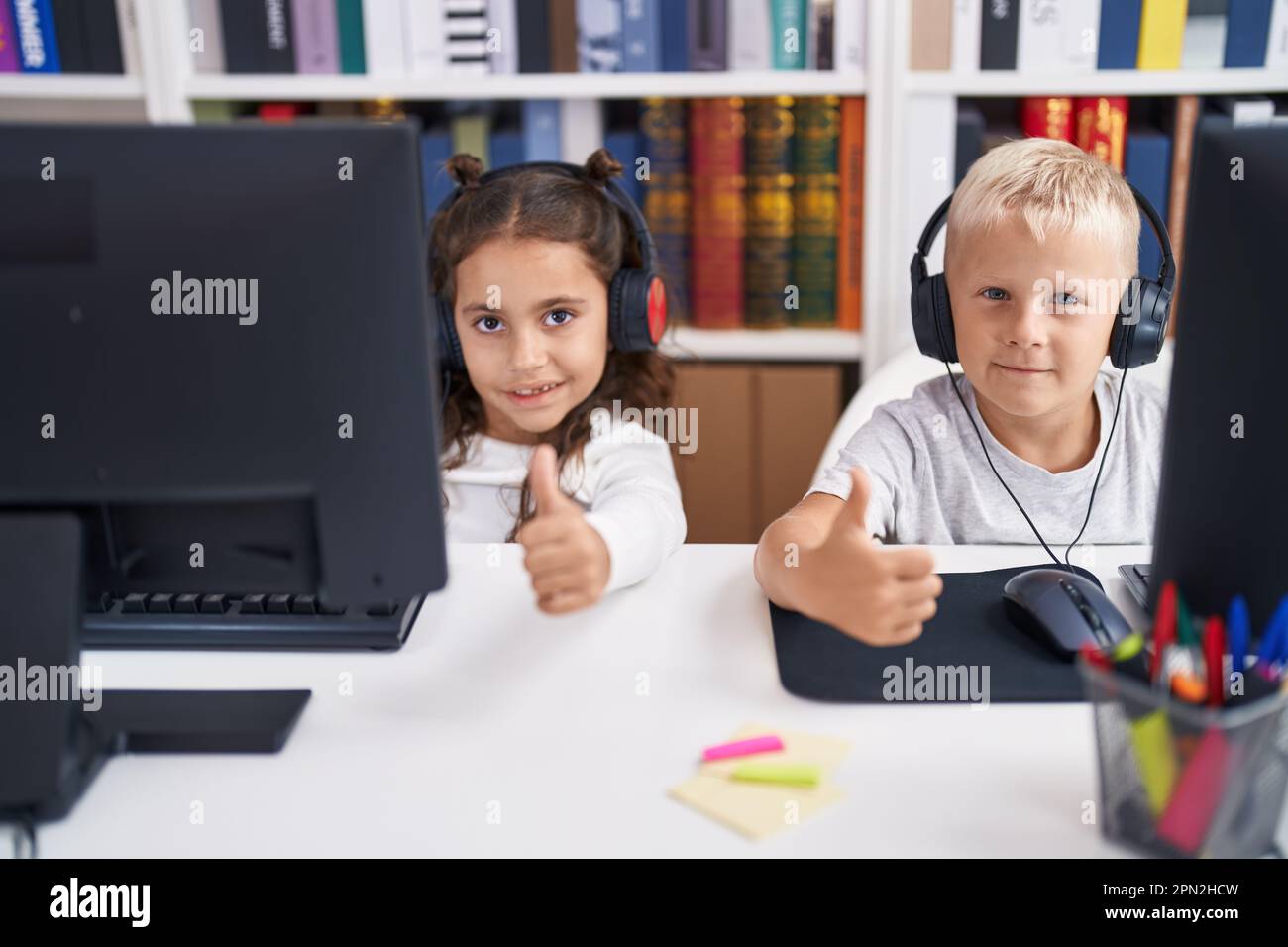 Adorable boy and girl students using computer and headphones doing ...