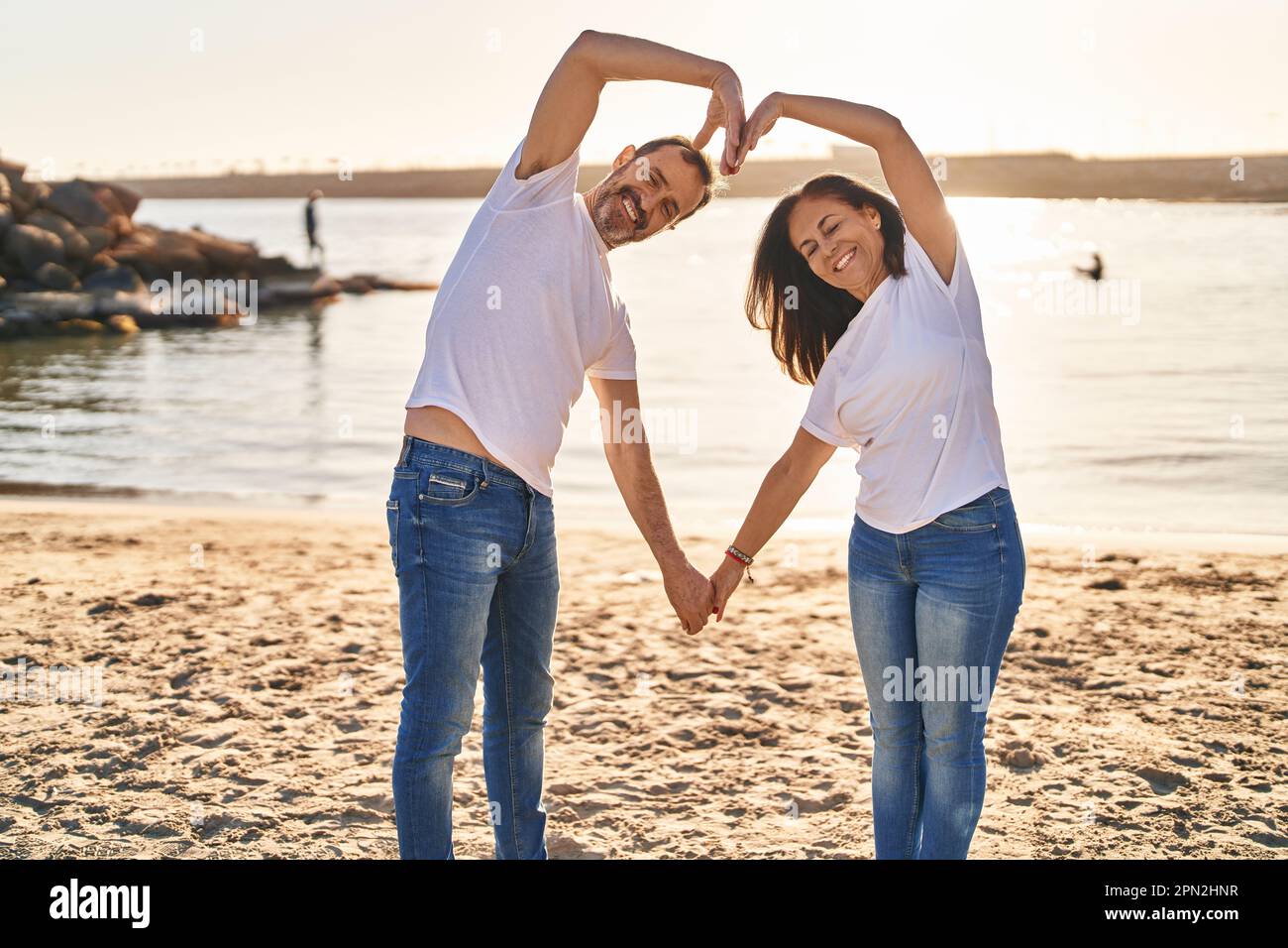 Middle age man and woman couple doing heart symbol with arms at seaside ...