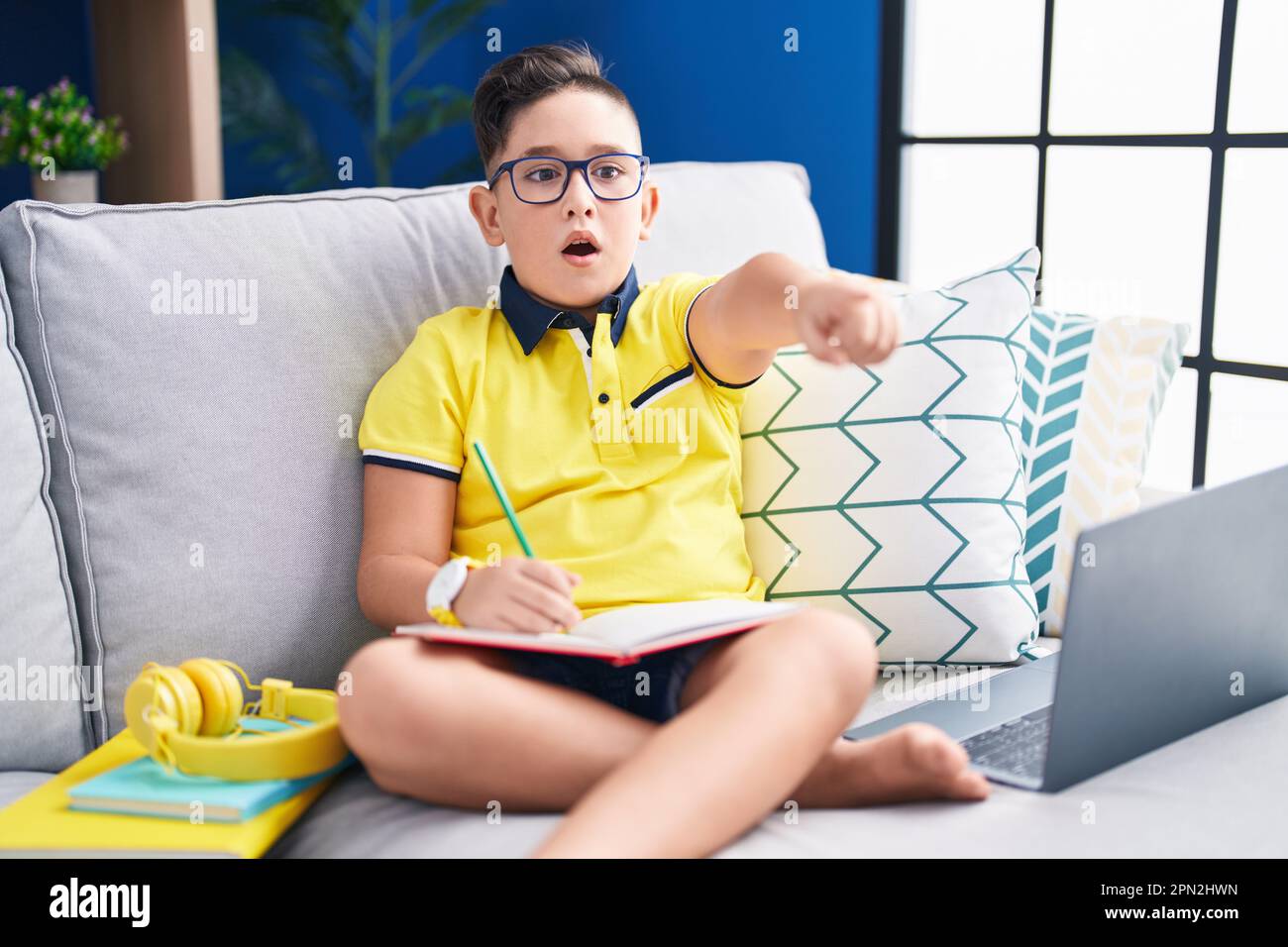 Young hispanic kid doing homework sitting on the sofa pointing with ...