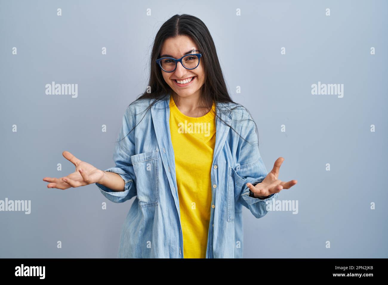 Young hispanic woman standing over blue background smiling cheerful ...