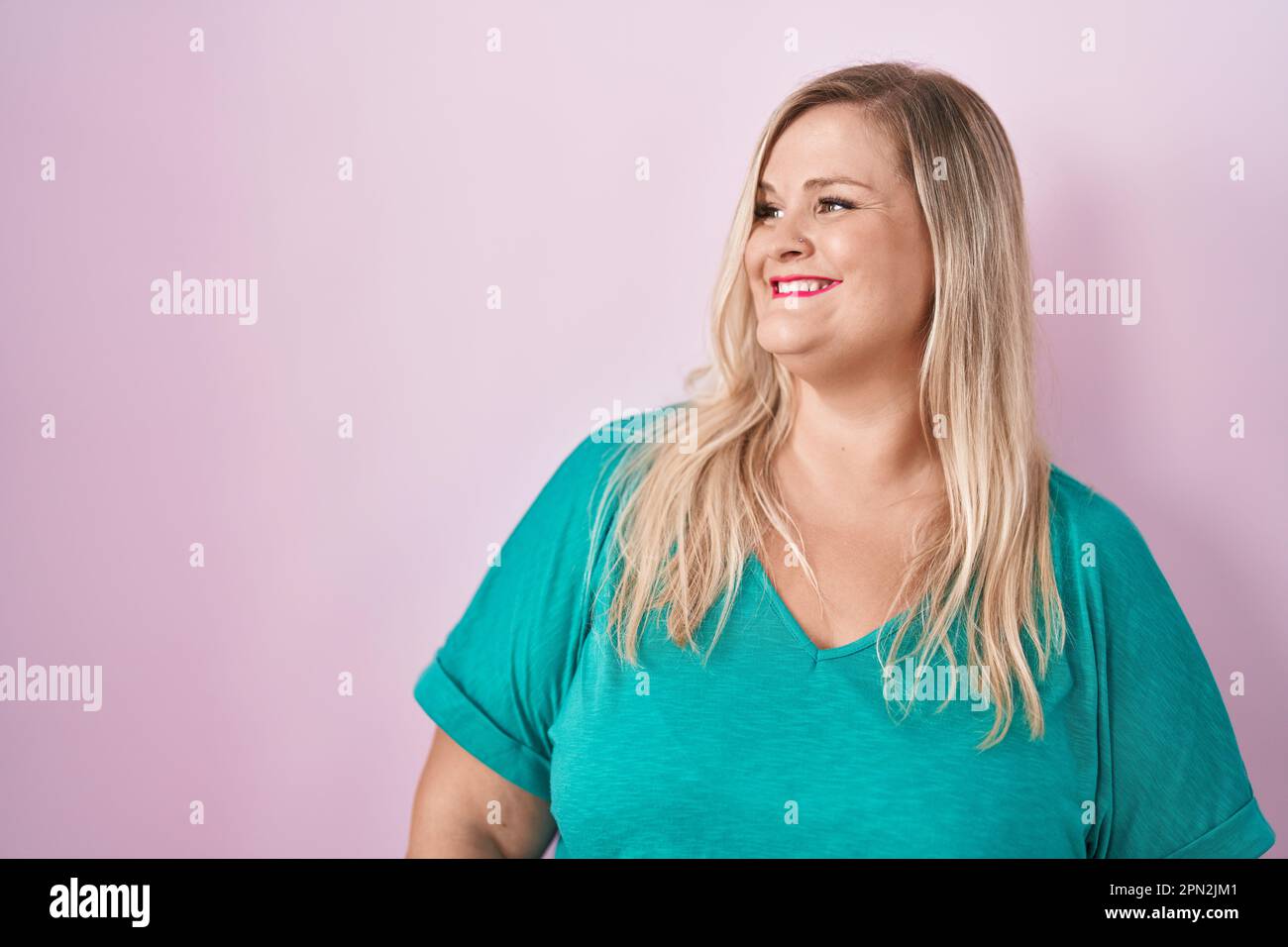 Caucasian plus size woman standing over pink background looking away to ...