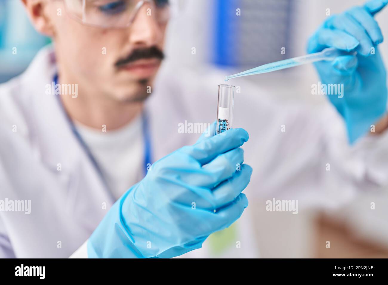 Young caucasian man scientist pouring liquid on test tube at laboratory ...